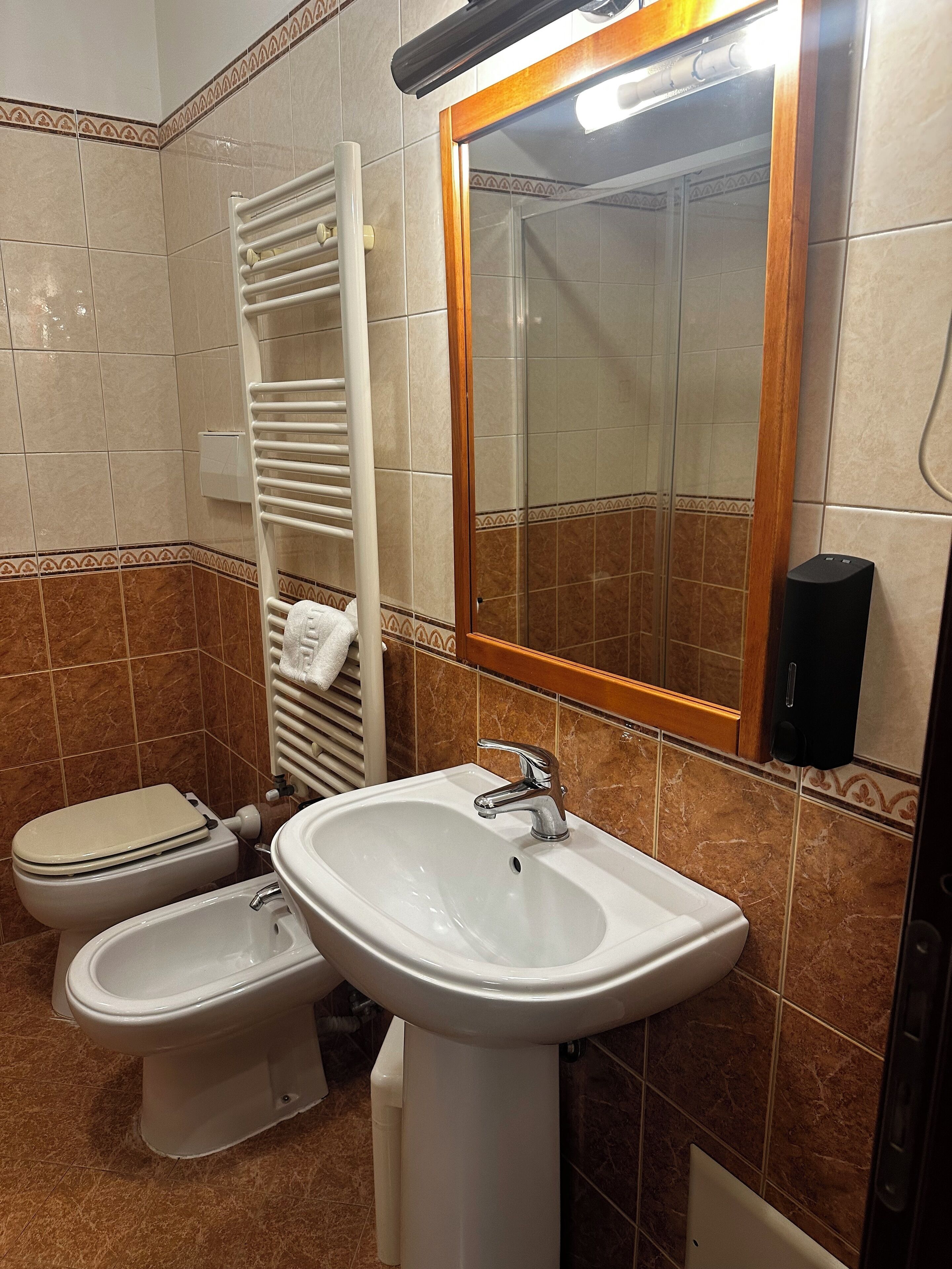 Casa de banho com sanita, bidé, lavatório, porta-toalhas, espelho e secador de mãos.