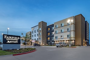 Um hotel Fairfield Inn & Suites Marriott com design moderno, vários andares e um estacionamento com veículos.