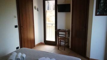 Quarto com cama, duas portas, uma cadeira, TV e varanda.