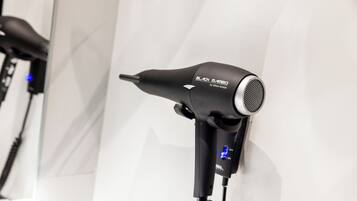 Secador de cabelo com visor digital e fio, fixado em parede branca.