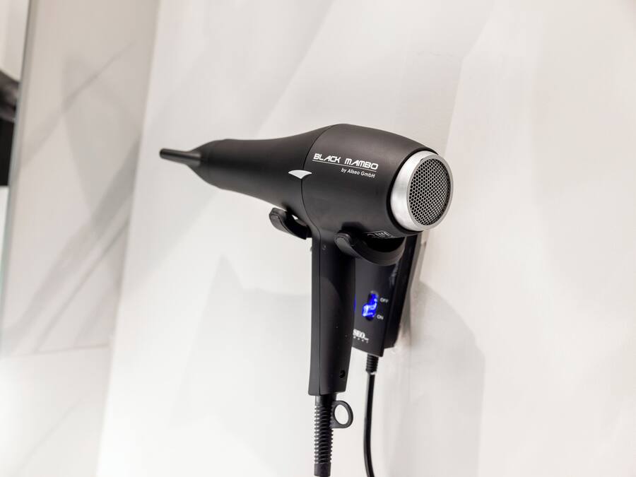 Secador de cabelo com visor digital e fio, fixado em parede branca.
