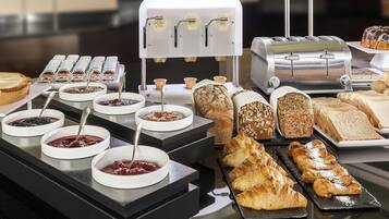 Buffet variado com diversas opções de acompanhamentos, incluindo Nutella, geleias e pão.
