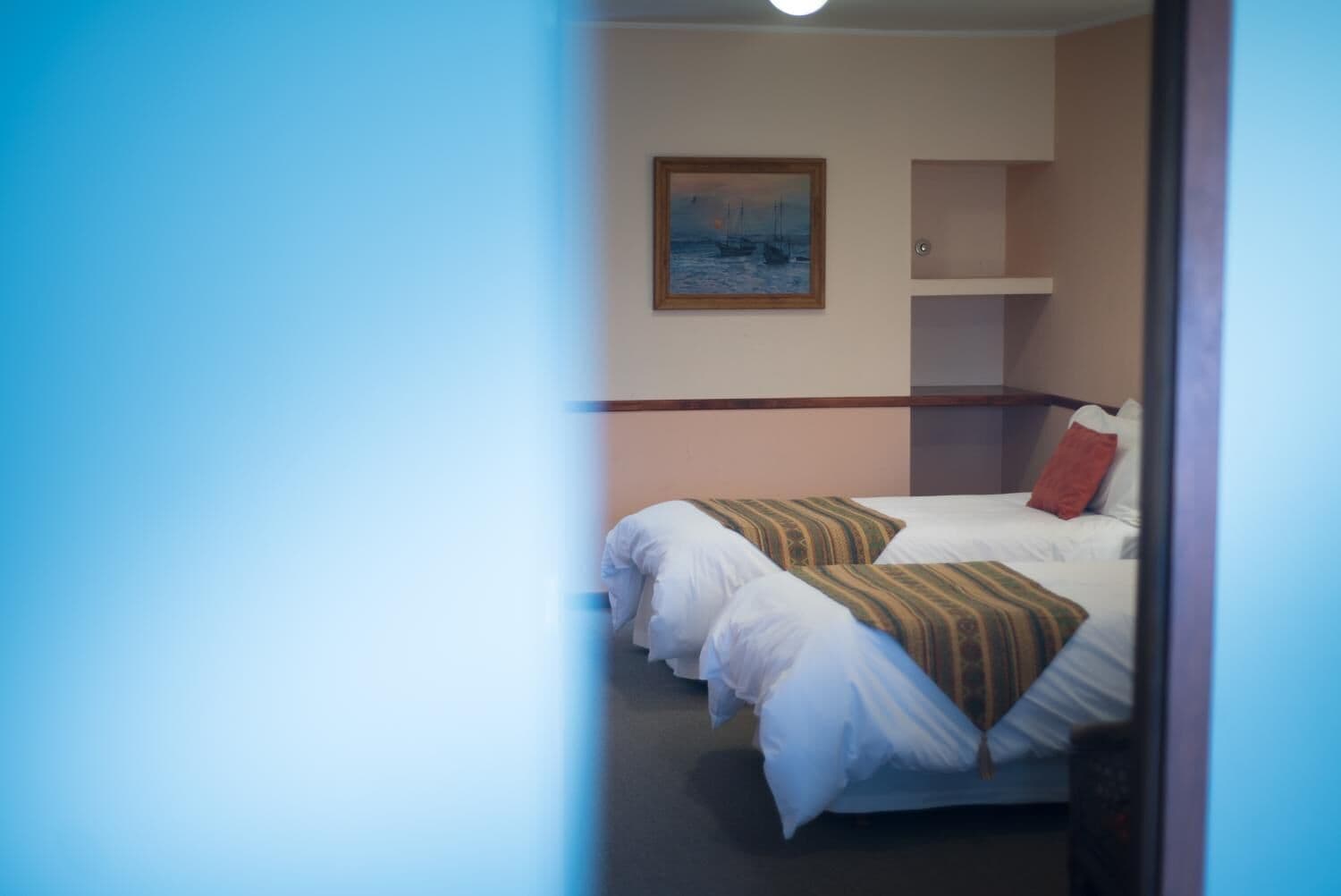 Quarto de hotel com duas camas, um quadro na parede e uma pequena estante.