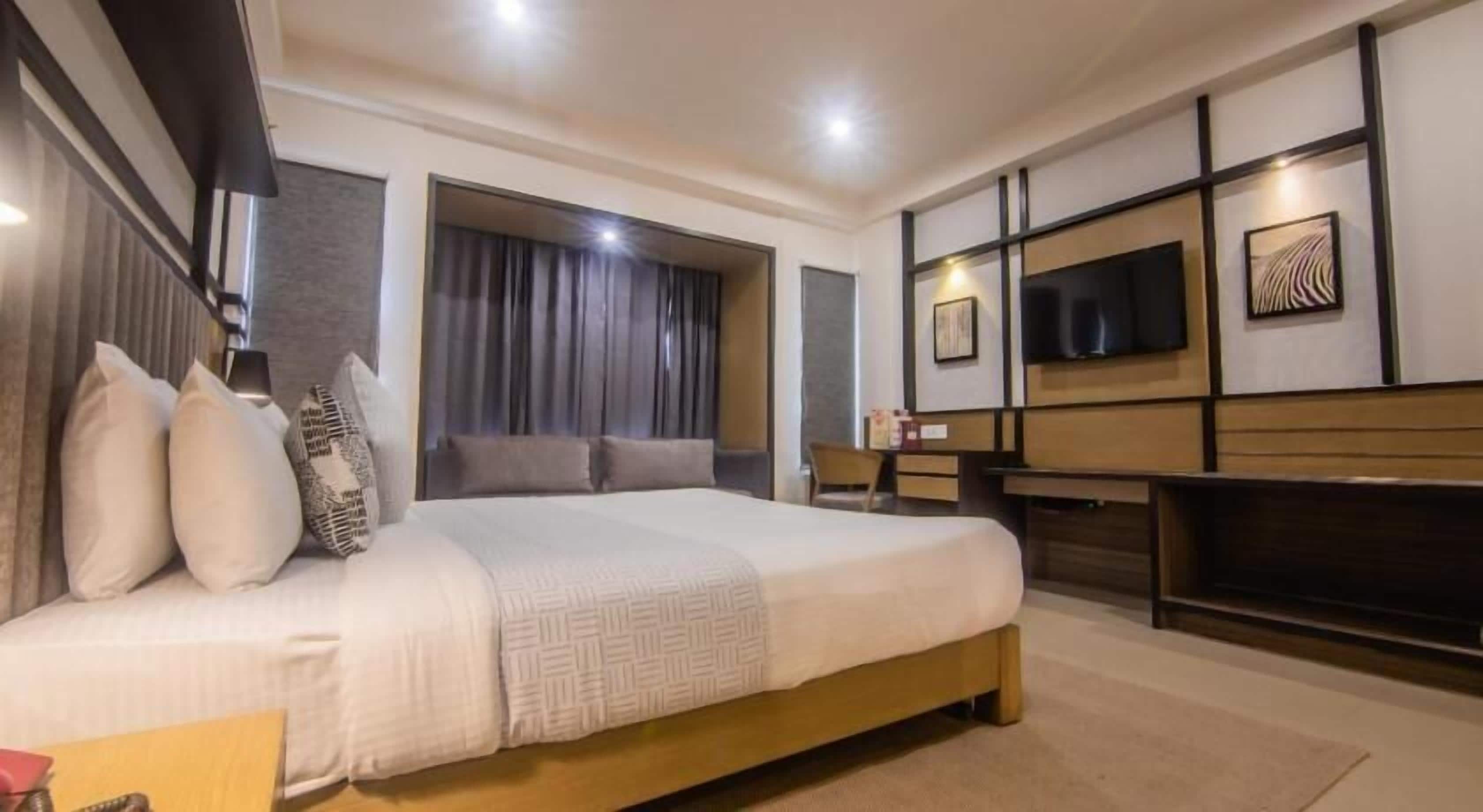 Quarto de hotel moderno com uma cama grande, televisão de tela plana, escrivaninha e área de estar.