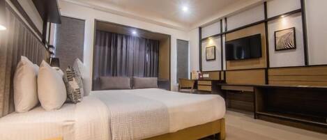Quarto de hotel moderno com uma cama grande, televisão de tela plana, escrivaninha e área de estar.