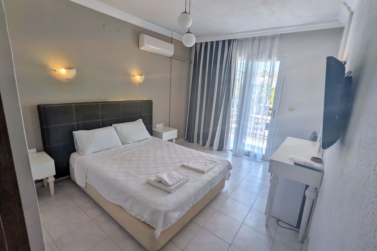 Quarto de hotel com uma cama grande, mesas de cabeceira, televisão de tela plana, janela com cortinas e uma varanda.