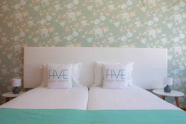 Uma cama de casal com duas almofadas, mesa de cabeceira, abajur e papel de parede floral.