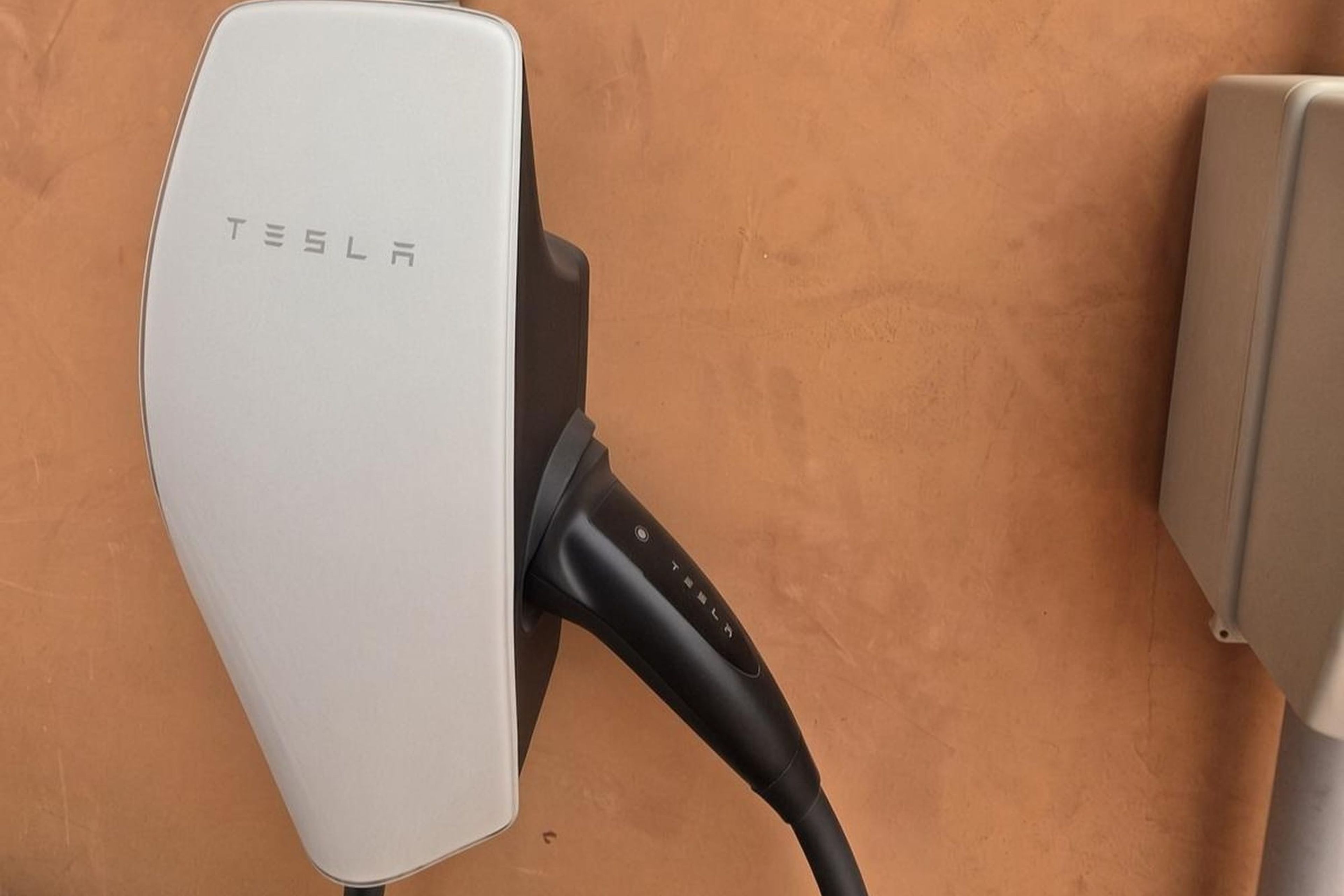 Estação de carregamento para veículos elétricos Tesla, com unidade de carregamento branca e cabo preto.