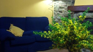 Um sofá azul com uma almofada, uma luminária e uma planta com flores amarelas.
