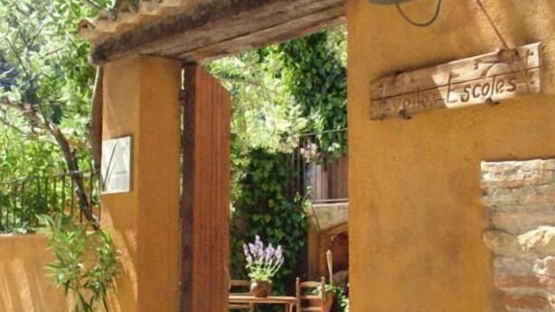 Um edifício rústico com parede de pedra, porta de madeira e uma placa com a inscrição 'Escuelas'.