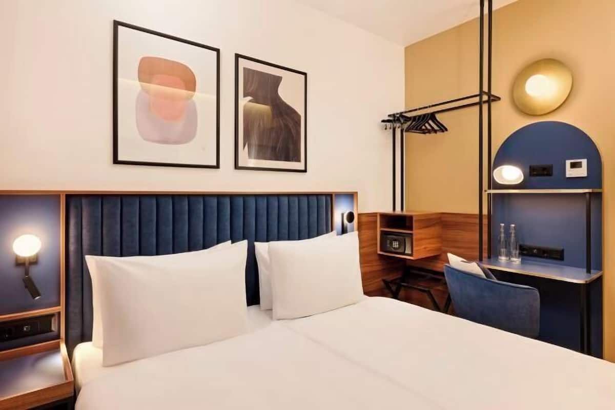 Quarto de hotel com cama, mesas de cabeceira, escrivaninha e uma cadeira.