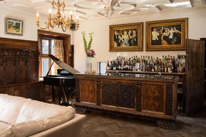 Um salão imponente com um piano, um bar repleto de garrafas e duas pinturas emolduradas na parede.