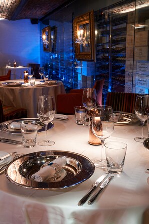 Ambiente de restaurante com mesas preparadas para refeições, com copos e talheres brilhantes.