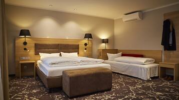 Quarto de hotel com duas camas, um banquinho marrom e duas luminárias de cabeceira.