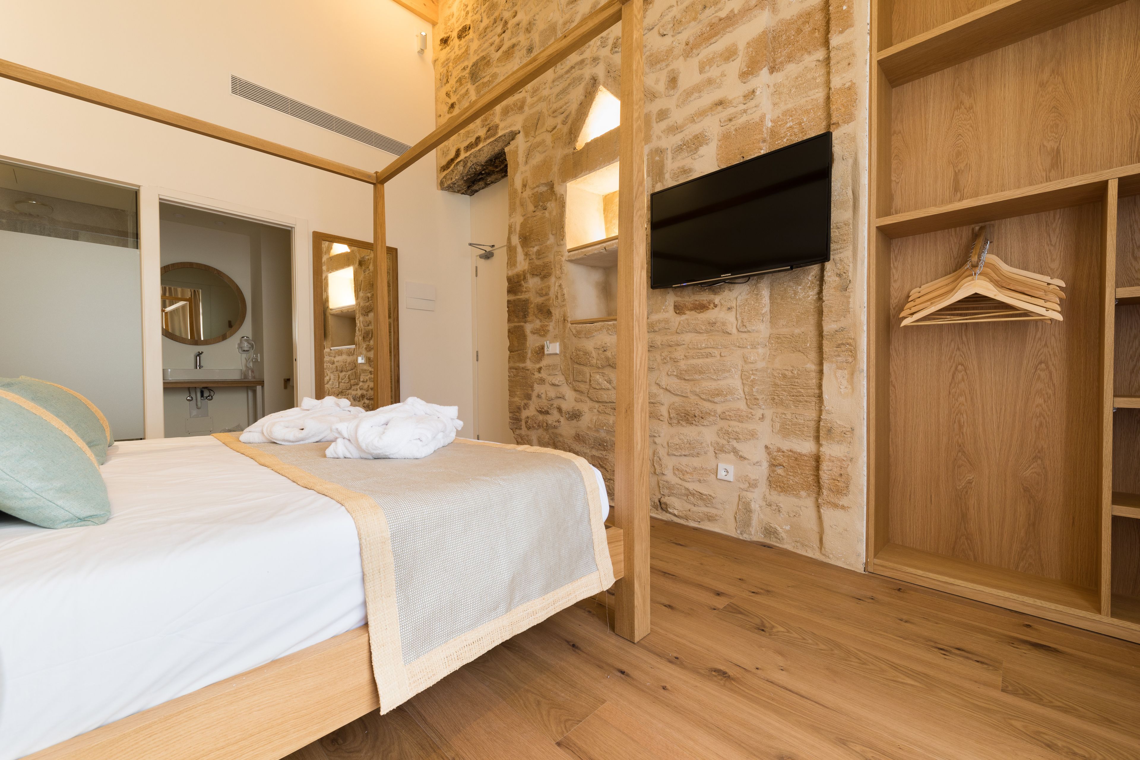 Quarto com cama, guarda-roupa de madeira e parede de pedra.