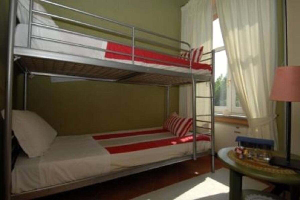Quarto com beliche, janela, cortinas e uma pequena mesa com abajur.