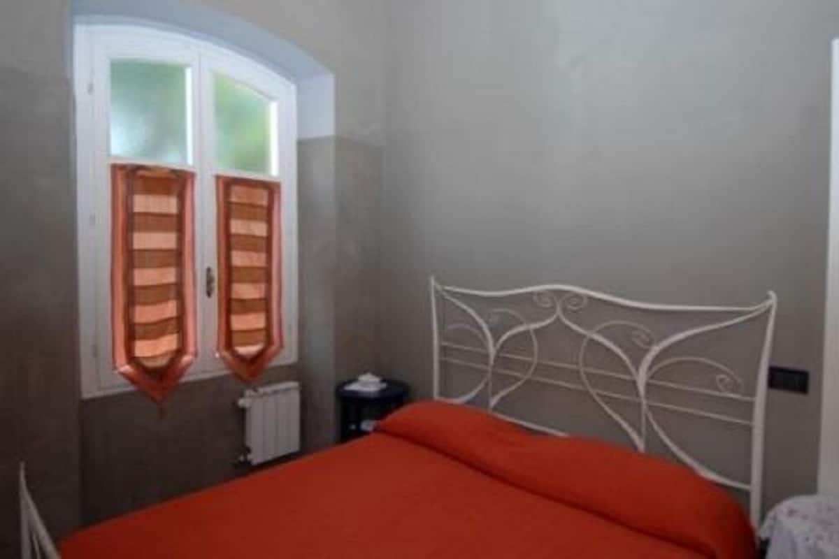 Quarto com cama, radiador e janela com portadas.