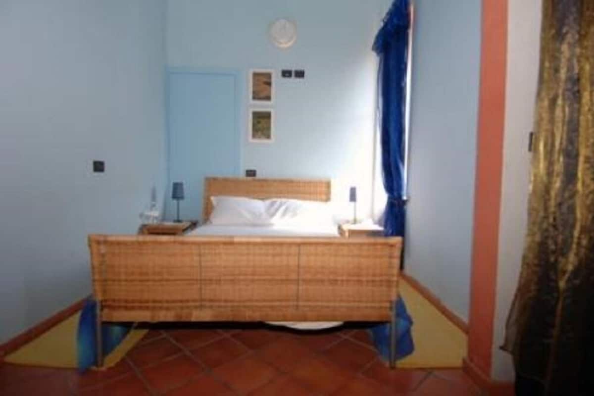 Quarto com uma cama, mesa de cabeceira, relógio na parede e uma porta.