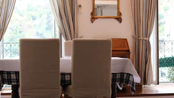 Quarto com duas cadeiras, uma cama com colcha xadrez, mesa de cabeceira de madeira, espelho na parede e janela com cortinas.