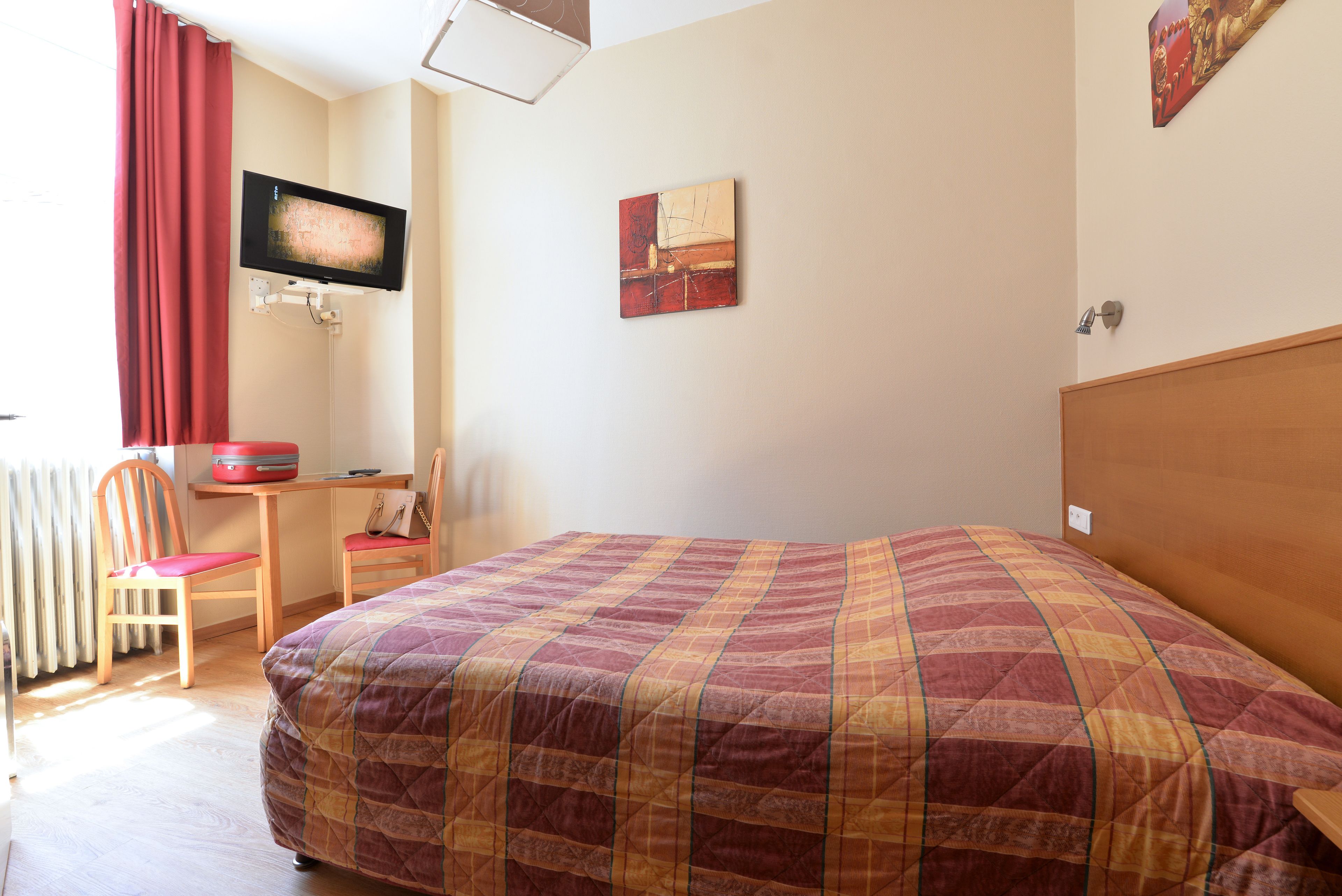 Quarto com cama, escrivaninha, cadeira, televisão e radiador.