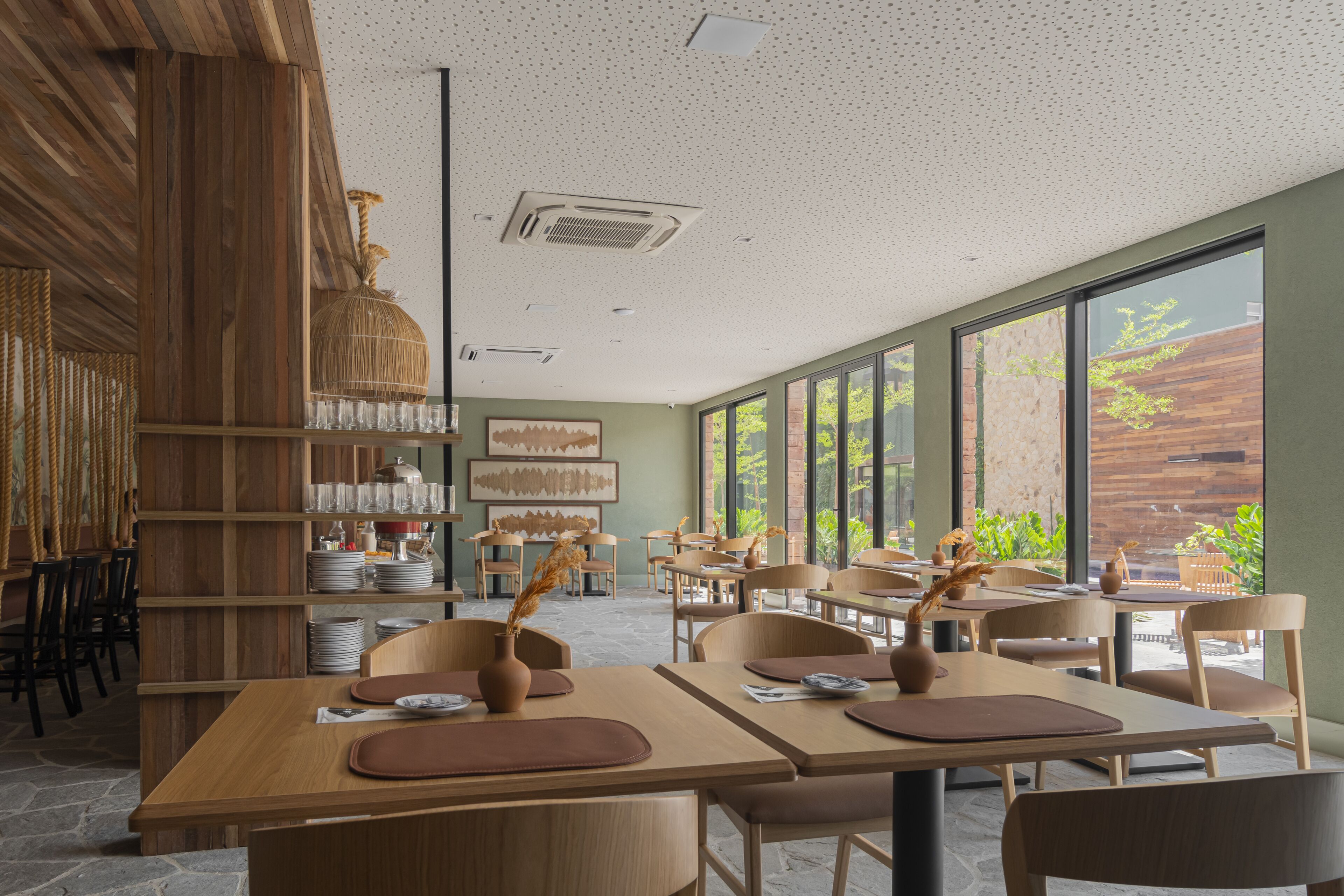 Um restaurante moderno com mesas e cadeiras de madeira, grandes janelas e chão de pedra.