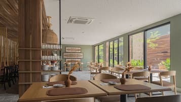 Um restaurante moderno com mesas e cadeiras de madeira, grandes janelas e chão de pedra.