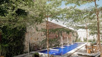 Uma área de piscina com mesa e cadeiras, cercada por vegetação e um muro de pedra.