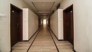 Um corredor comprido e estreito, com portas de madeira em ambos os lados e chão ladrilhado.