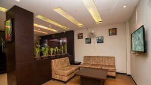 Um lobby moderno com um sofá, uma mesa de centro e um balcão de recepção decorado com plantas em vasos.