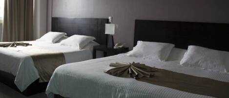 Quarto de hotel com duas camas, uma mesa de cabeceira, um abajur e um quadro na parede.
