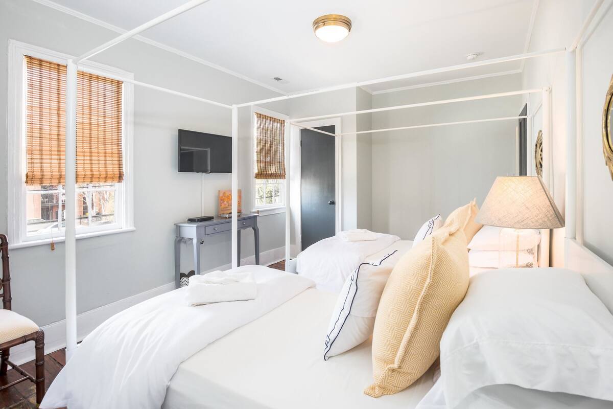 Quarto com cama, mesa de cabeceira, abajur e escrivaninha com cadeira.