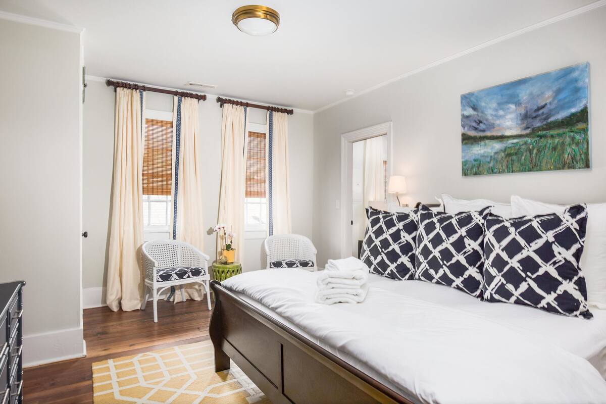 Quarto com cama, uma cadeira, mesa de cabeceira e um quadro na parede.