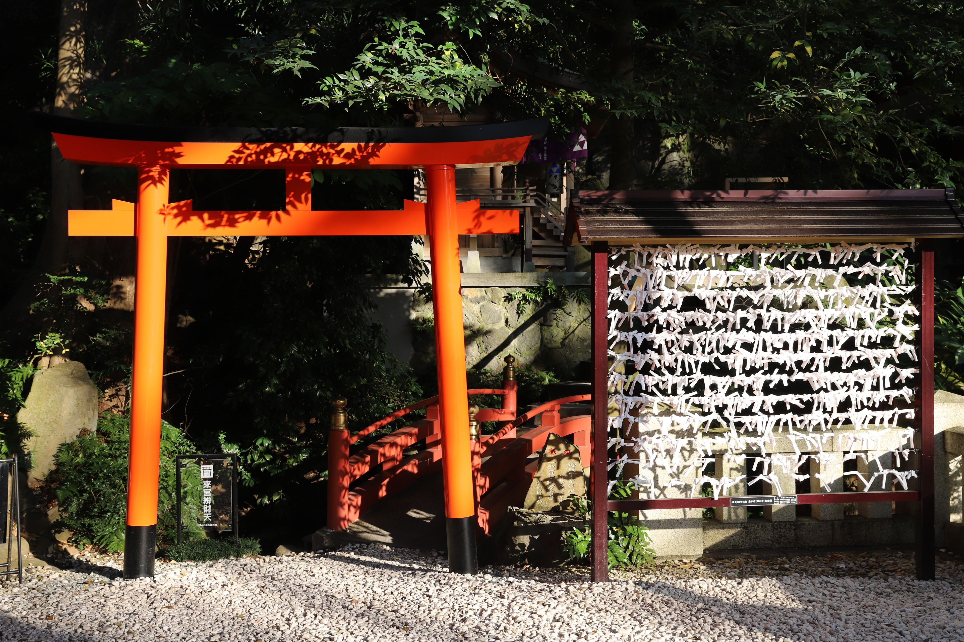 Um tradicional portão torii japonês, com base de pedra e estrutura superior de madeira, cercado por cascalho e vegetação.