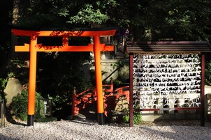 Um tradicional portão torii japonês, com base de pedra e estrutura superior de madeira, cercado por cascalho e vegetação.