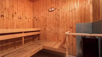 Uma sala de sauna com bancos de madeira, incluindo um banco com apoio para os pés, e um aquecedor de sauna.