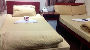 Quarto de hotel com duas camas, cada uma com roupa de cama e almofadas bege. Há uma pequena mesa de escritório com um telefone e uma tomada.