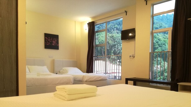 Quarto de hotel com duas camas de solteiro, uma cama de casal e varanda com vista para a floresta.