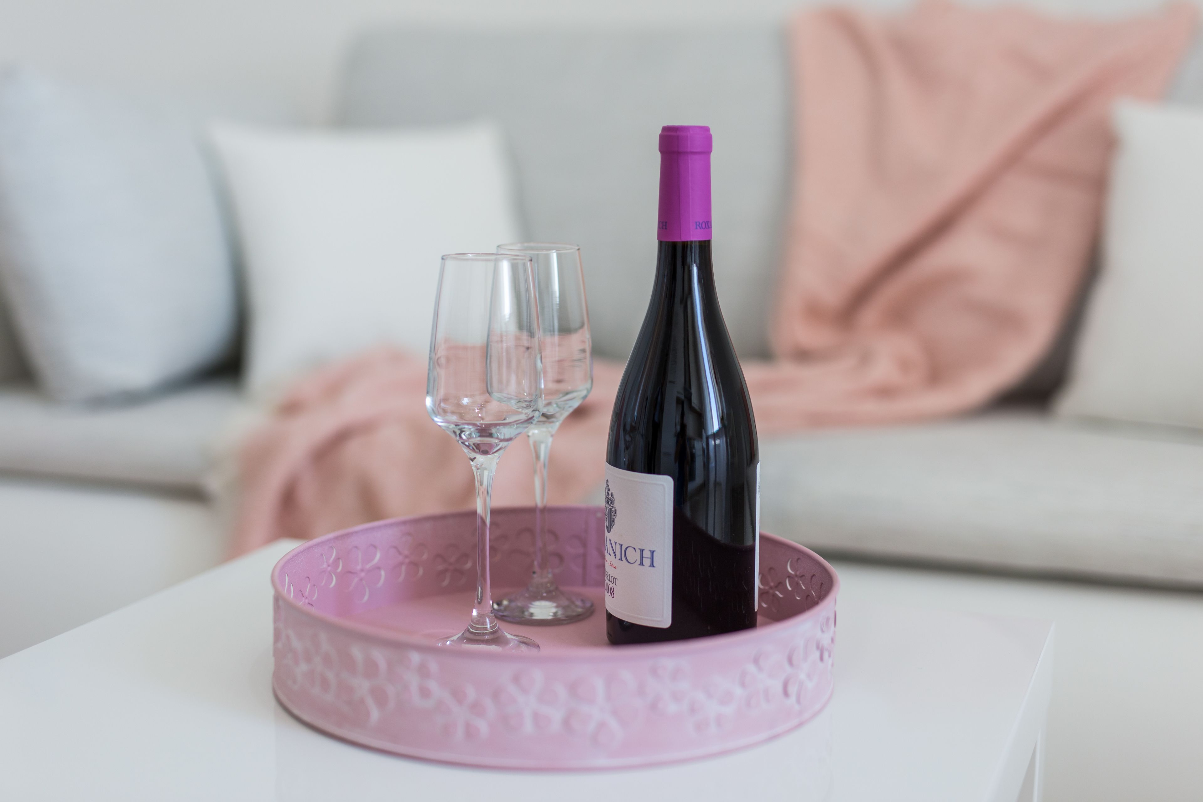 Uma garrafa de vinho e dois copos sobre um tabuleiro rosa em uma mesa branca.