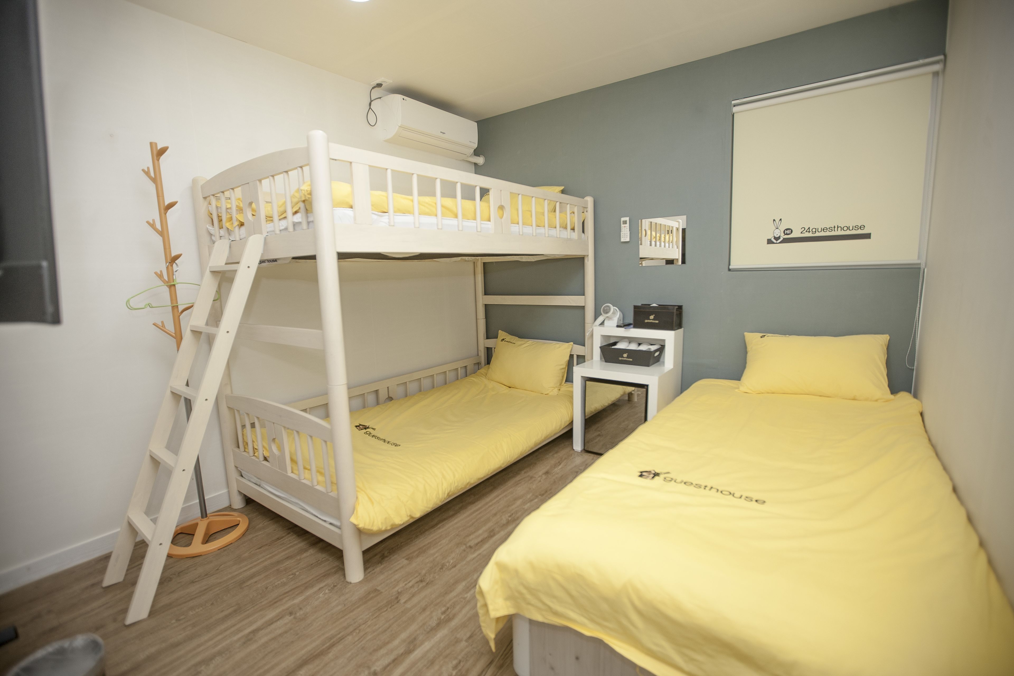 Quarto com beliche, duas camas, um criado-mudo e um projetor fixado na parede.