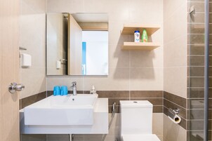 Casa de banho moderna com lavatório duplo, sanita e espelho. Existem duas prateleiras sobre o lavatório com artigos de higiene pessoal.