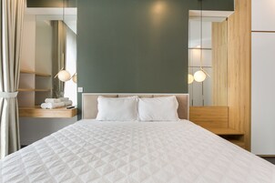 Cama bem arrumada com um edredom branco acolchoado, cabeceira de madeira e duas luminárias de mesa.