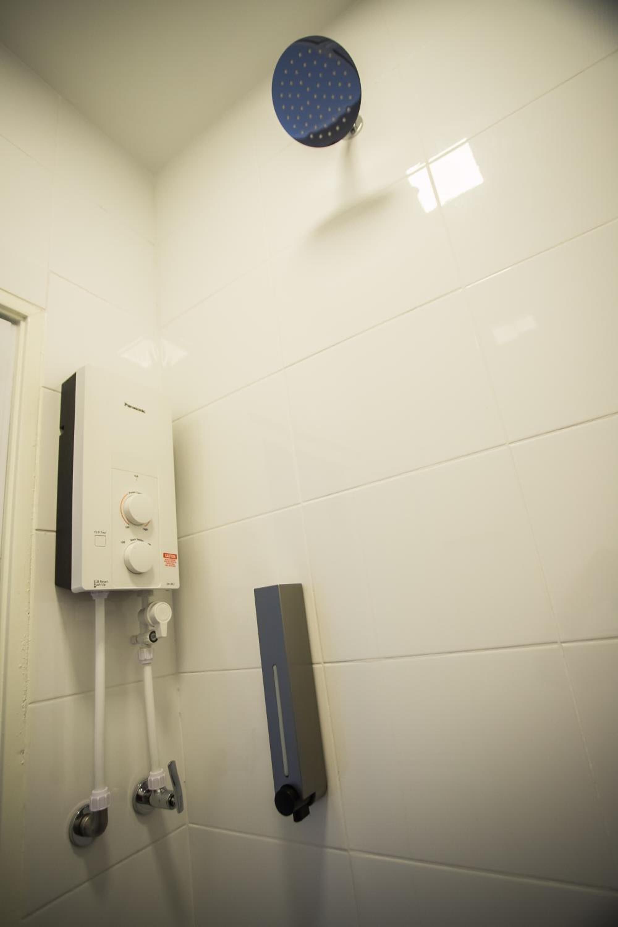 Um banheiro com parede de azulejos brancos, aquecedor de água branco e chuveiro azul.