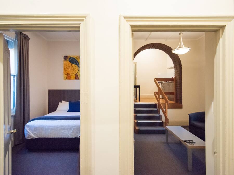 Quarto de hotel com uma cama, um quadro na parede, uma escada e um espaço de estar com uma mesa.