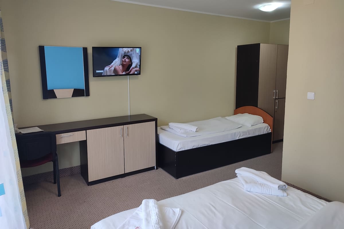 Quarto de hotel com cama, escrivaninha, cadeira, guarda-roupa e televisão.