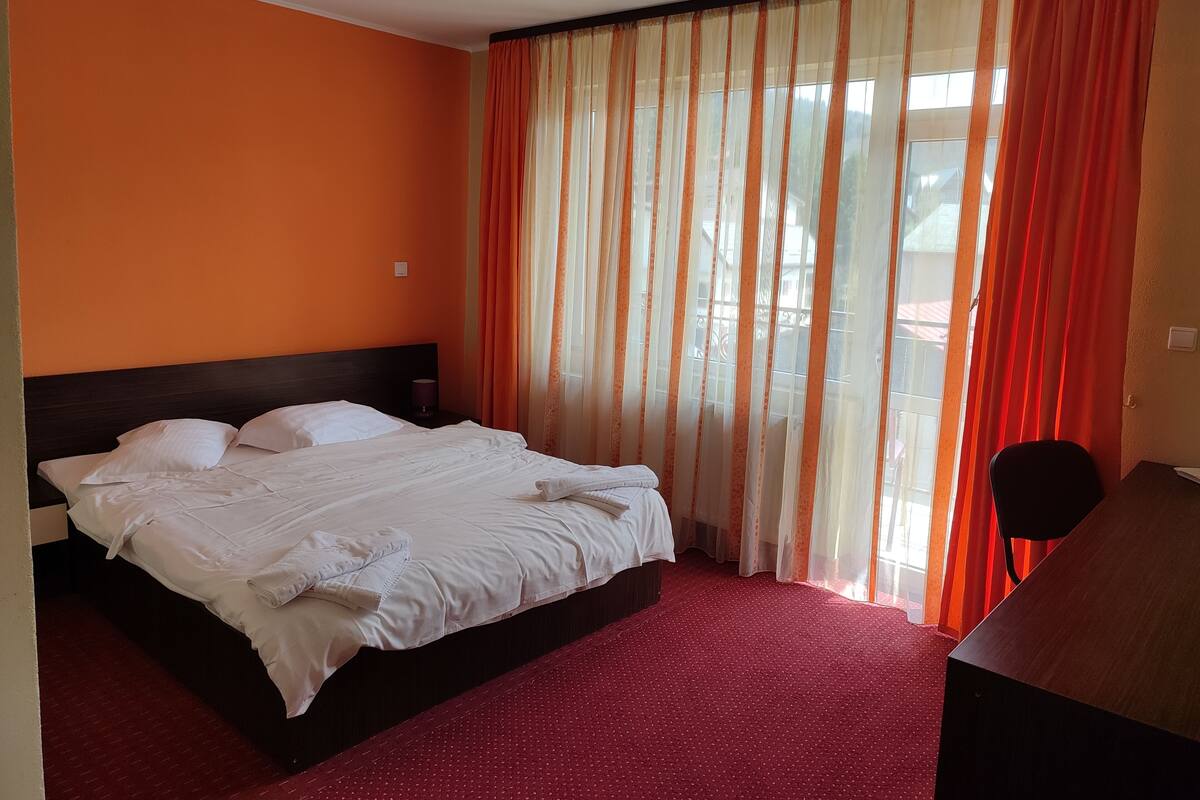 Quarto de hotel com cama, escrivaninha e janela com cortinas.