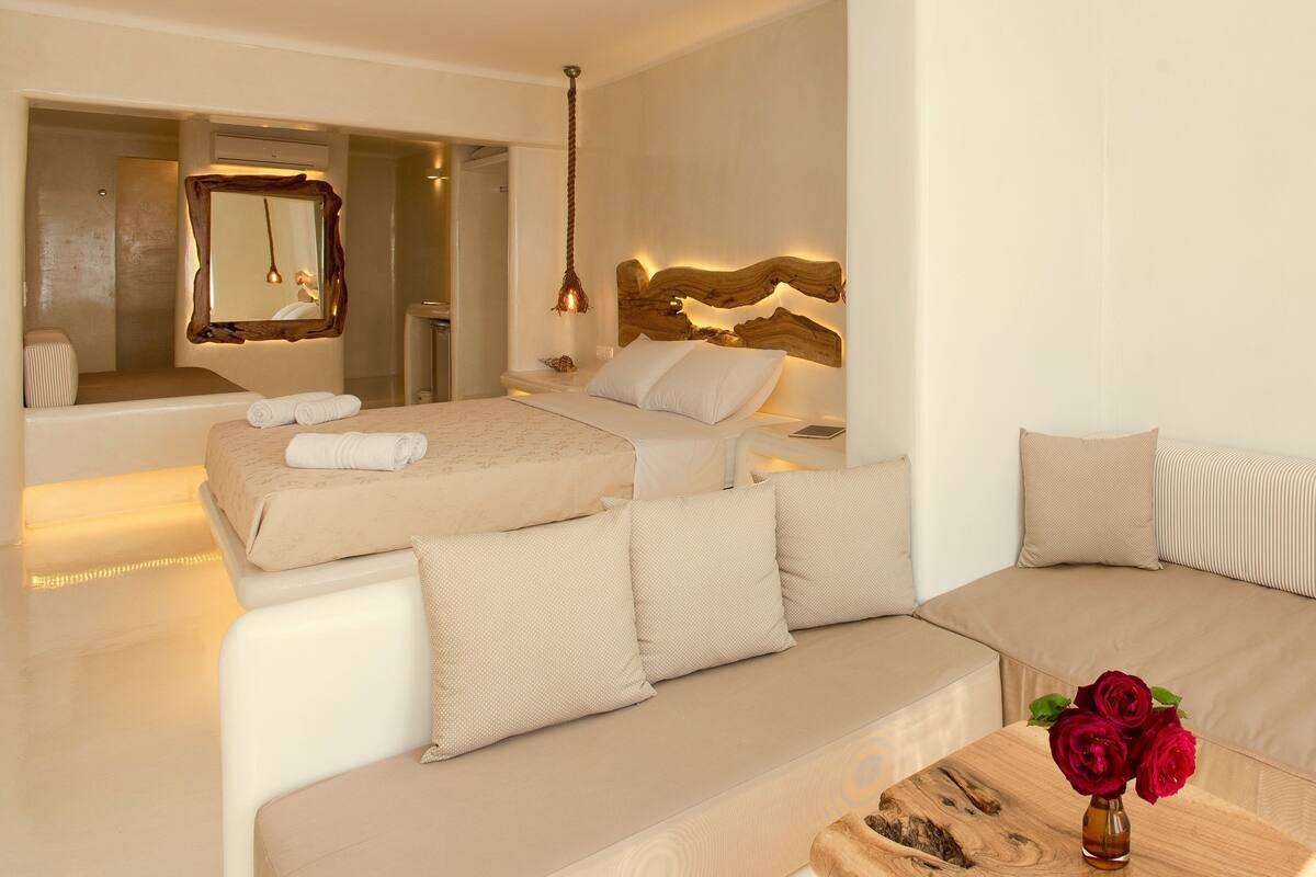 Quarto moderno com uma cama, um sofá, cabeceira de madeira, um espelho e um vaso com flores.