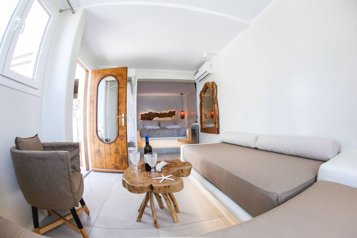Quarto moderno e bem iluminado com sofá, mesa de madeira com garrafa e copos, e um espelho grande.