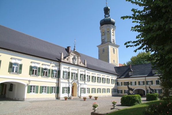 Um edifício histórico com um pátio central, uma torre com cúpula e uma estátua de um cavalo.