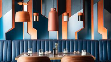 Interior moderno de restaurante com parede estampada em padrão geométrico, mesa redonda de madeira e duas cadeiras.