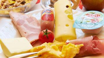 Um prato de café da manhã com diversos alimentos, incluindo ovos, presunto, queijo e um tomate.